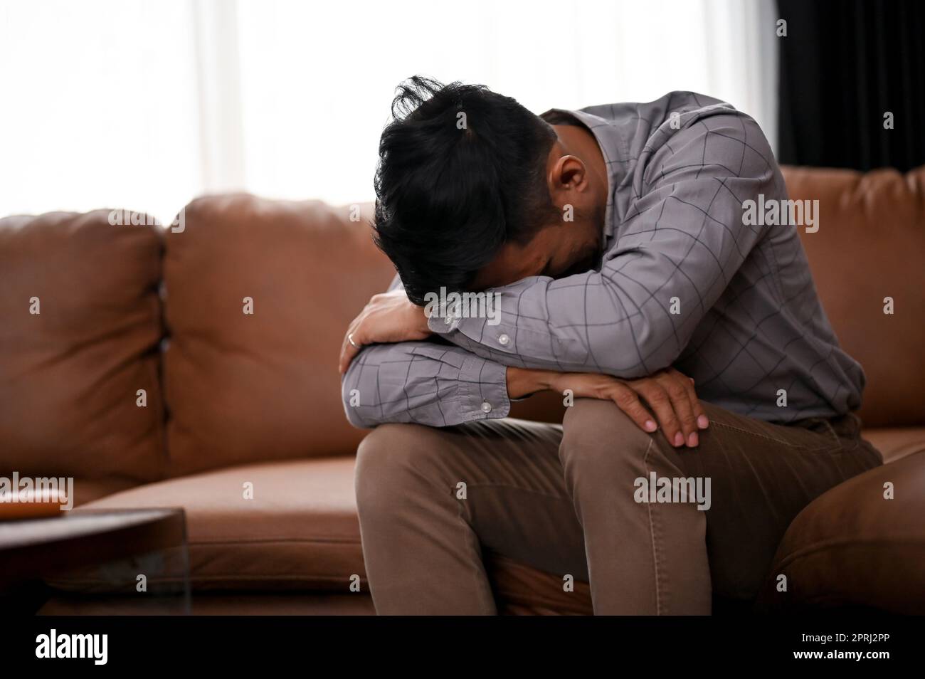 Stressed and depressed millennial Asian man is crying on the sofa in a ...