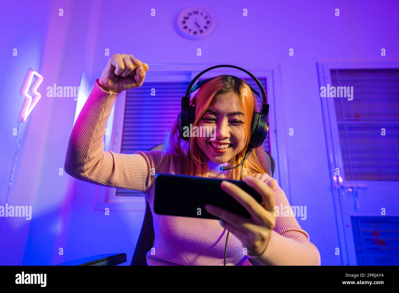 Happy Gamer playing video game online with smartphone she raises hands ...