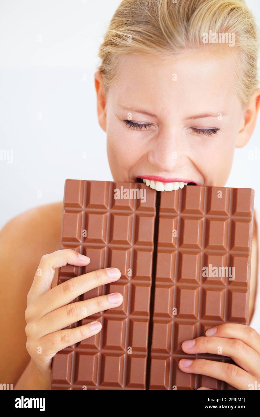 Overdoing it - Indulgences. Young woman biting into a huge bar of ...