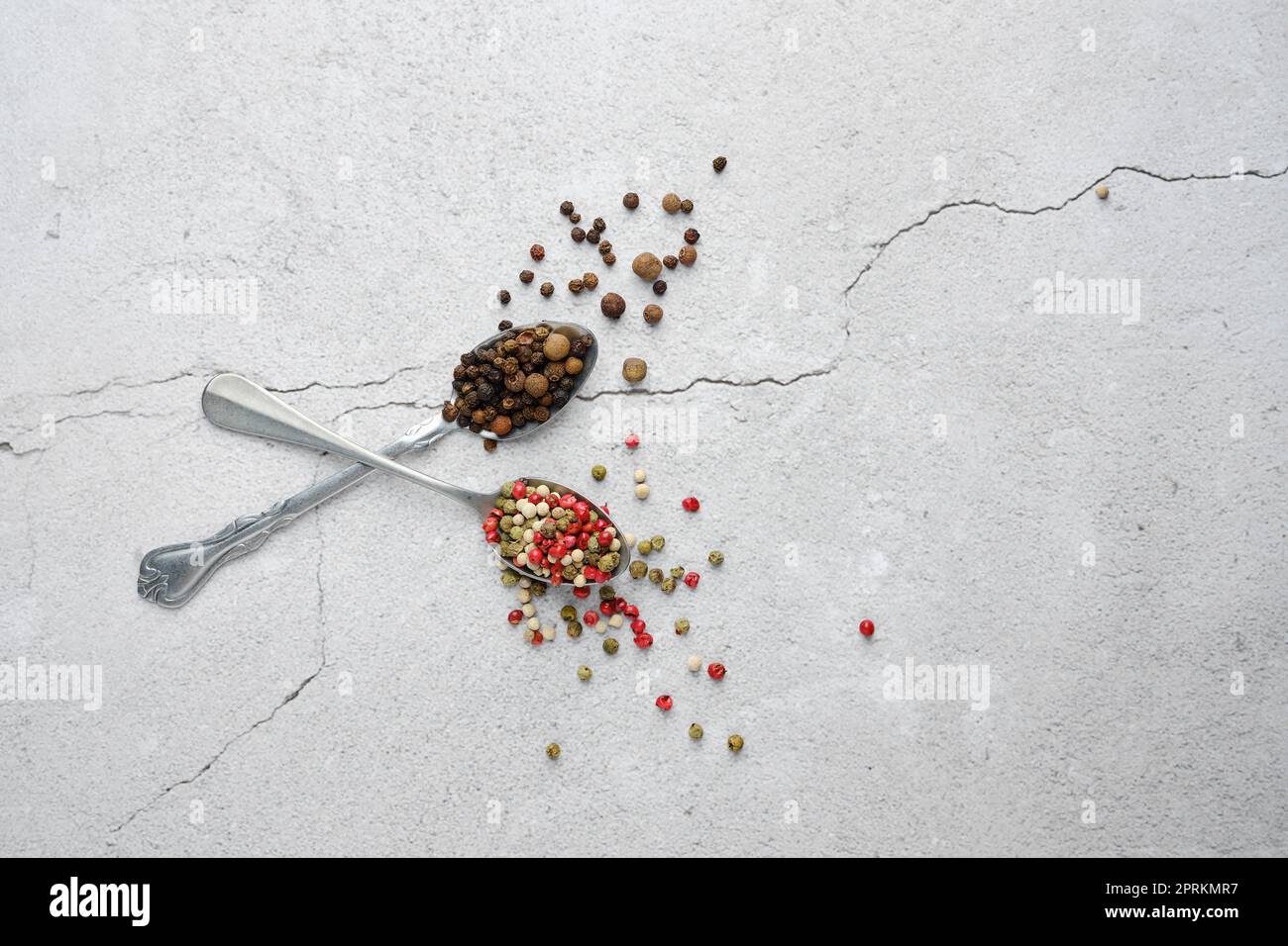 Two crossed spoons with different kinds of pepper on concrete ...
