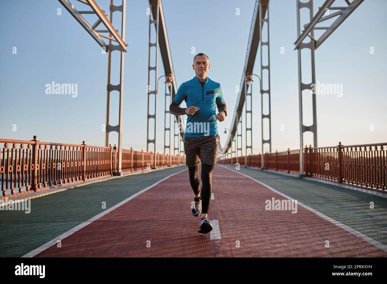Portrait of attractive fit man running fast along big modern bridge ...