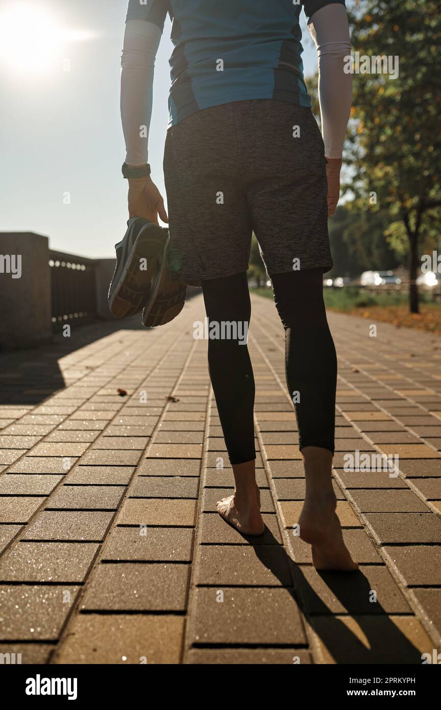 Man runner holding sport shoes walking on waterfront. Back view crop ...
