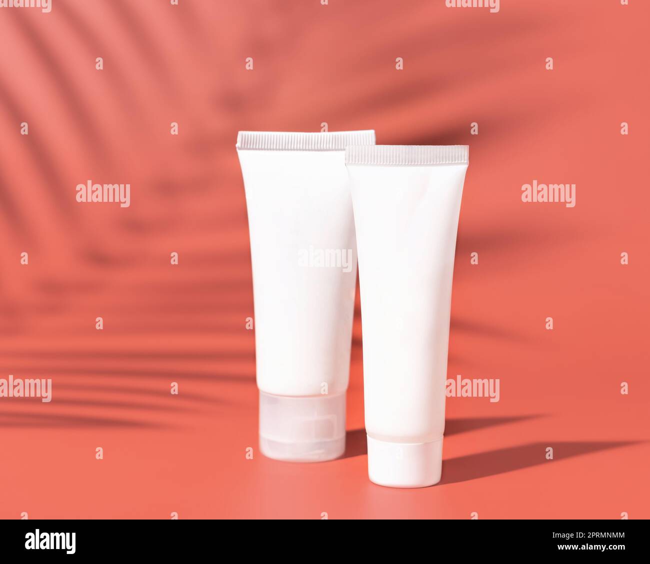 Two plastic cream tubes on pink, Palm leaf hard shadows. Cosmetic ...