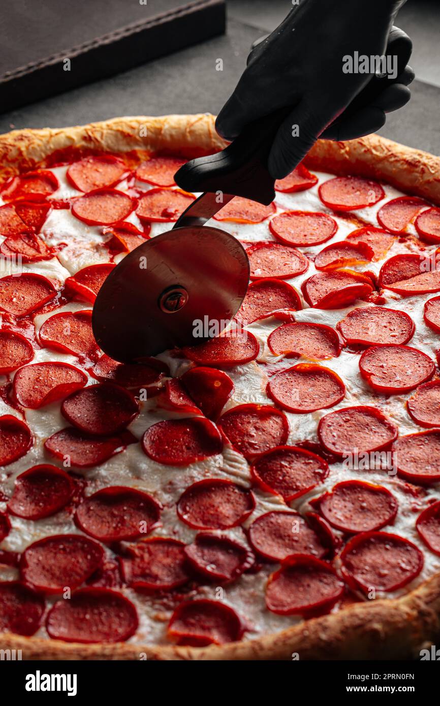 Cutting giant pepperoni pizza with special knife Stock Photo - Alamy