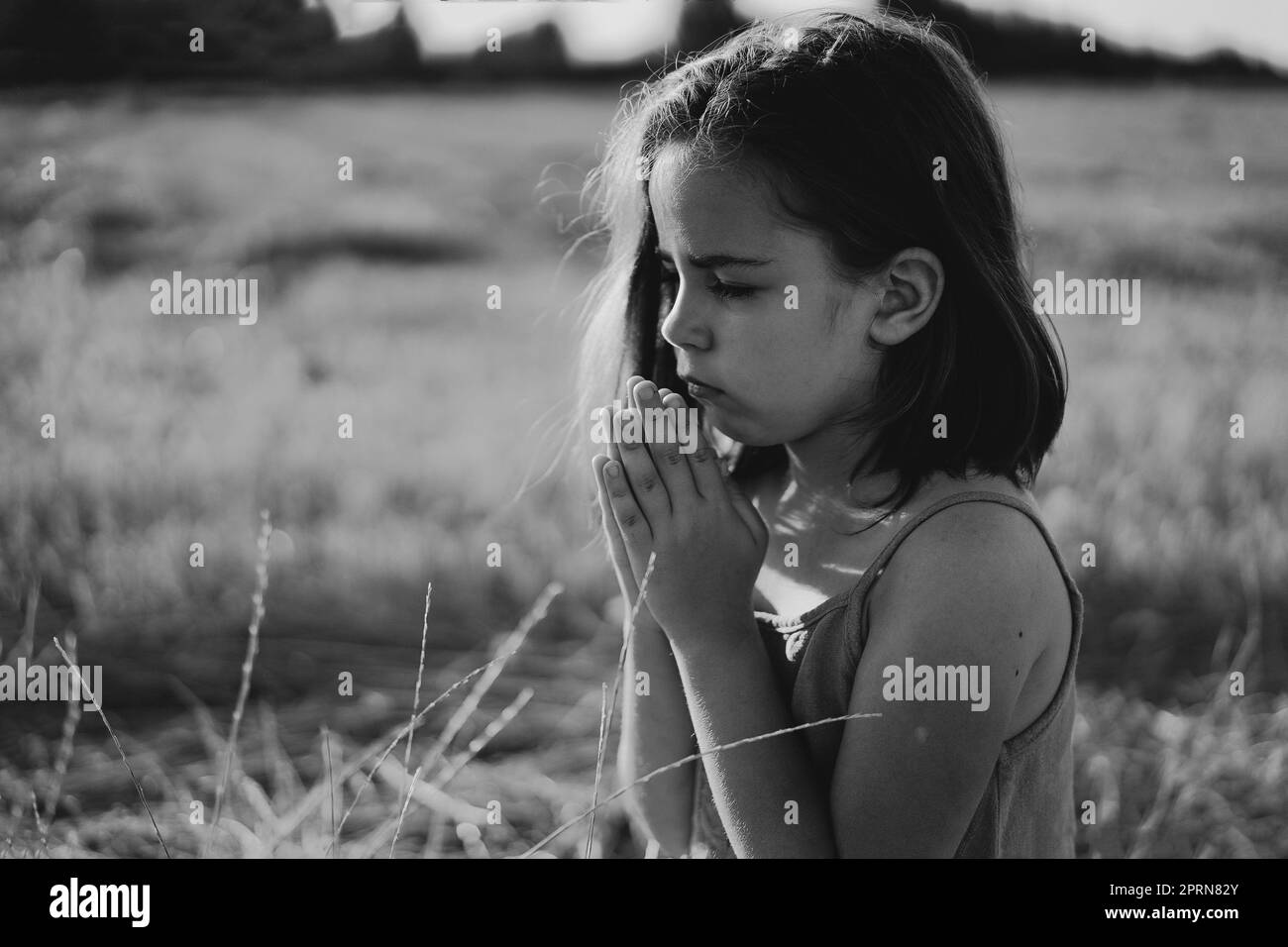 Little Girl closed her eyes, praying in a field. Hands folded in prayer ...