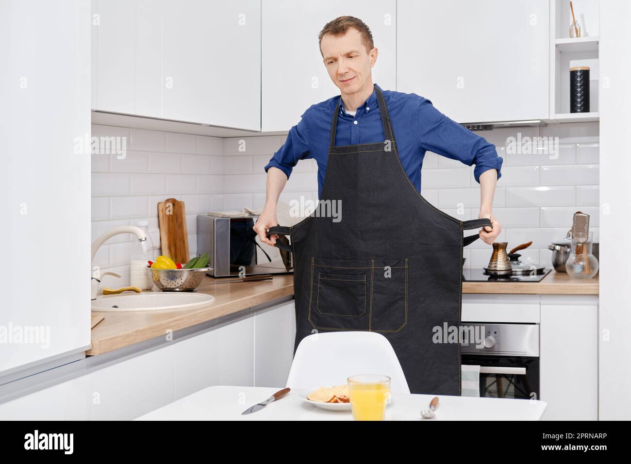 Mid adult man takes off his apron before eating the breakfast he has ...