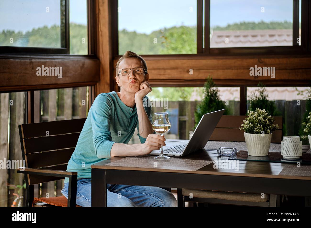 Funny man sits behind the table with laptop, drinks wine and giving an ...