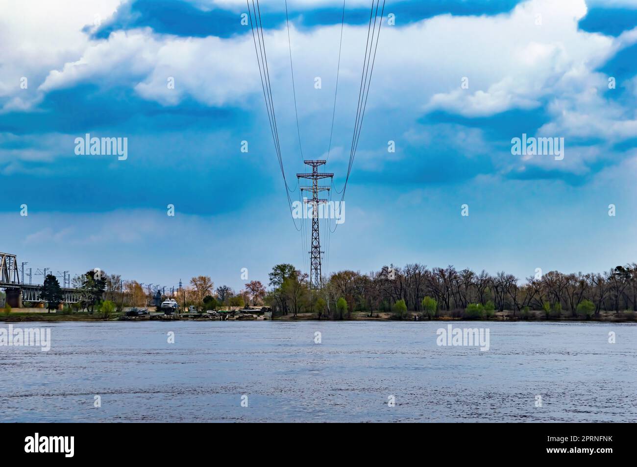 Wires of a high-voltage power line tower over a river. Electric wire ...