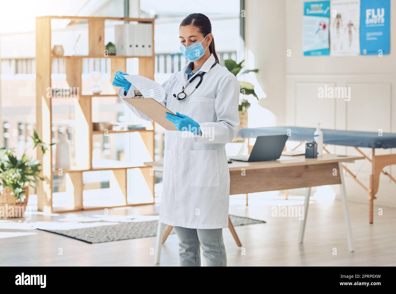 Medical doctor with a clipboard and face mask in her office reading ...