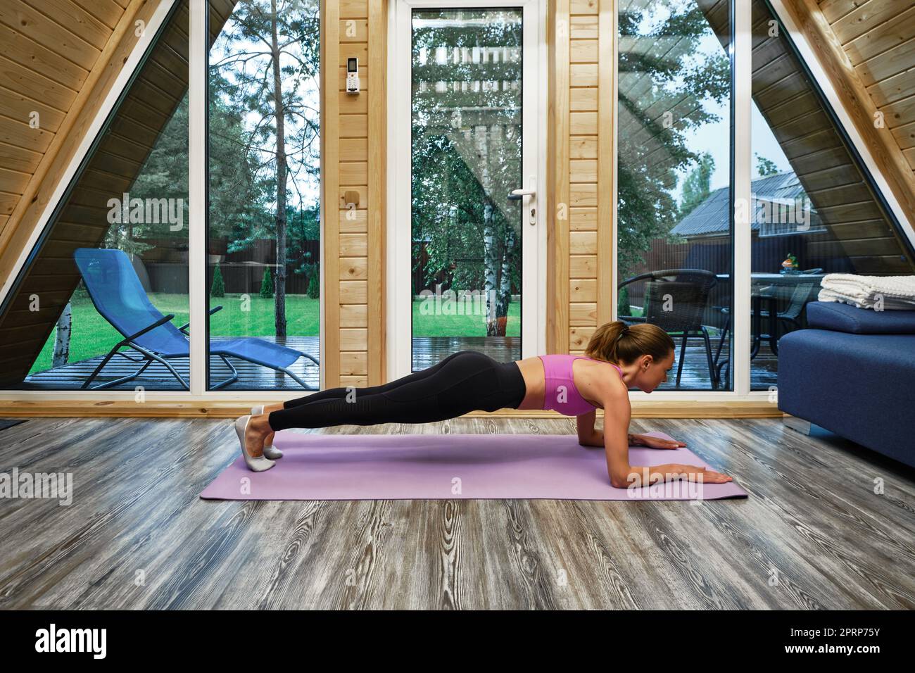 Sportive woman does plank exercise in forest cabin during the rain ...
