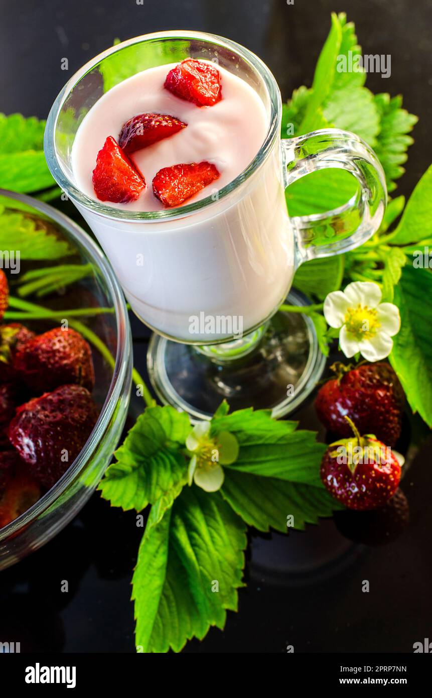 strawberry yoghurt and berries and flowers of a strawberry on a dark ...