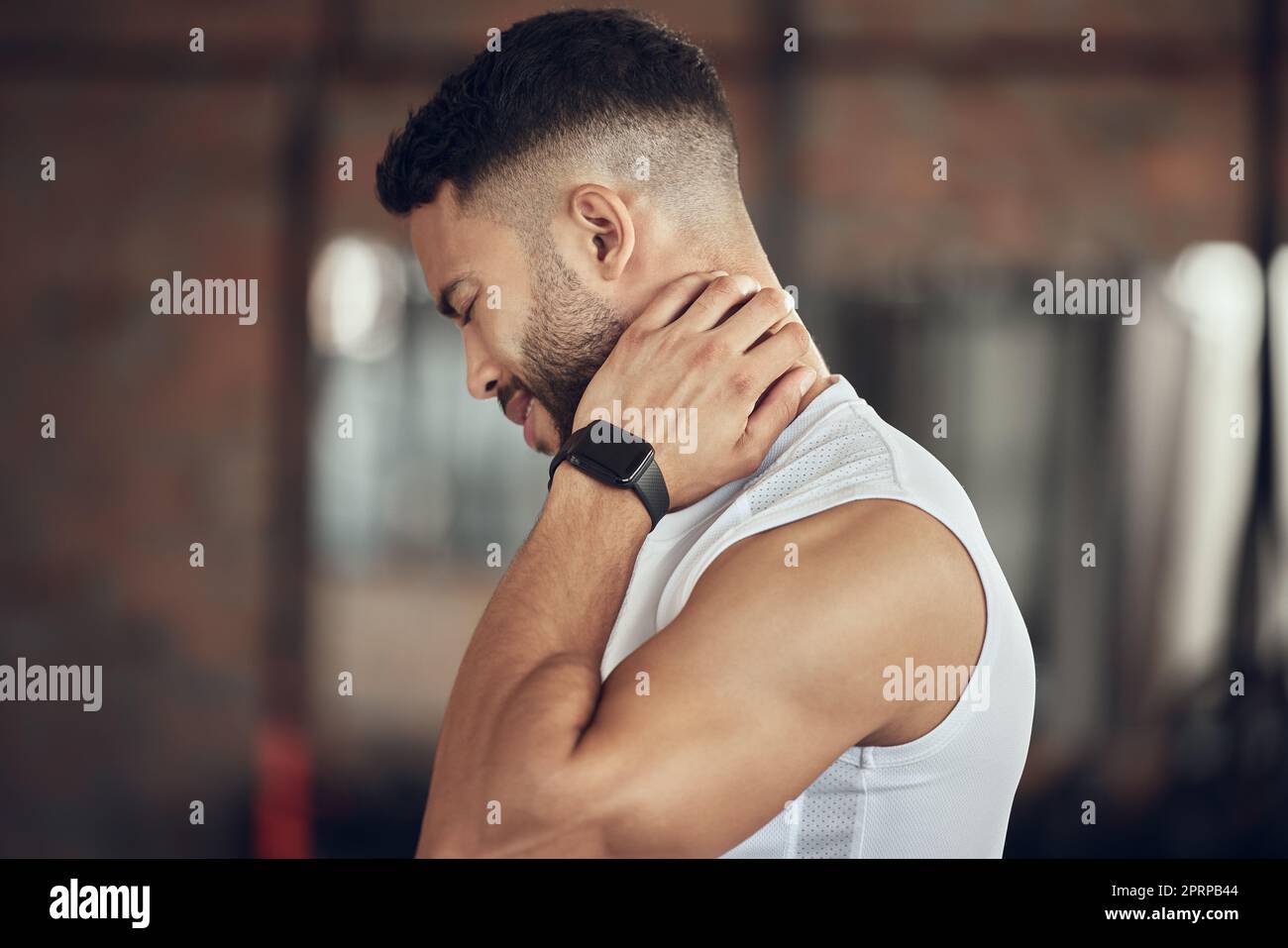 Young man with neck pain in the gym. Fit athlete with a stiff neck in ...