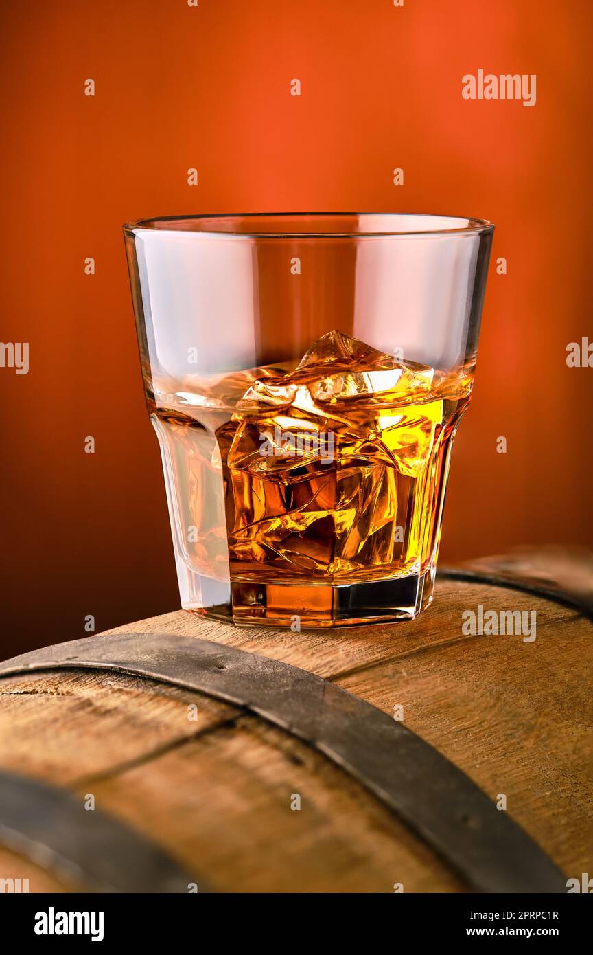 Glass of whisky with ice on the top of barrel (soft focus photo with ...