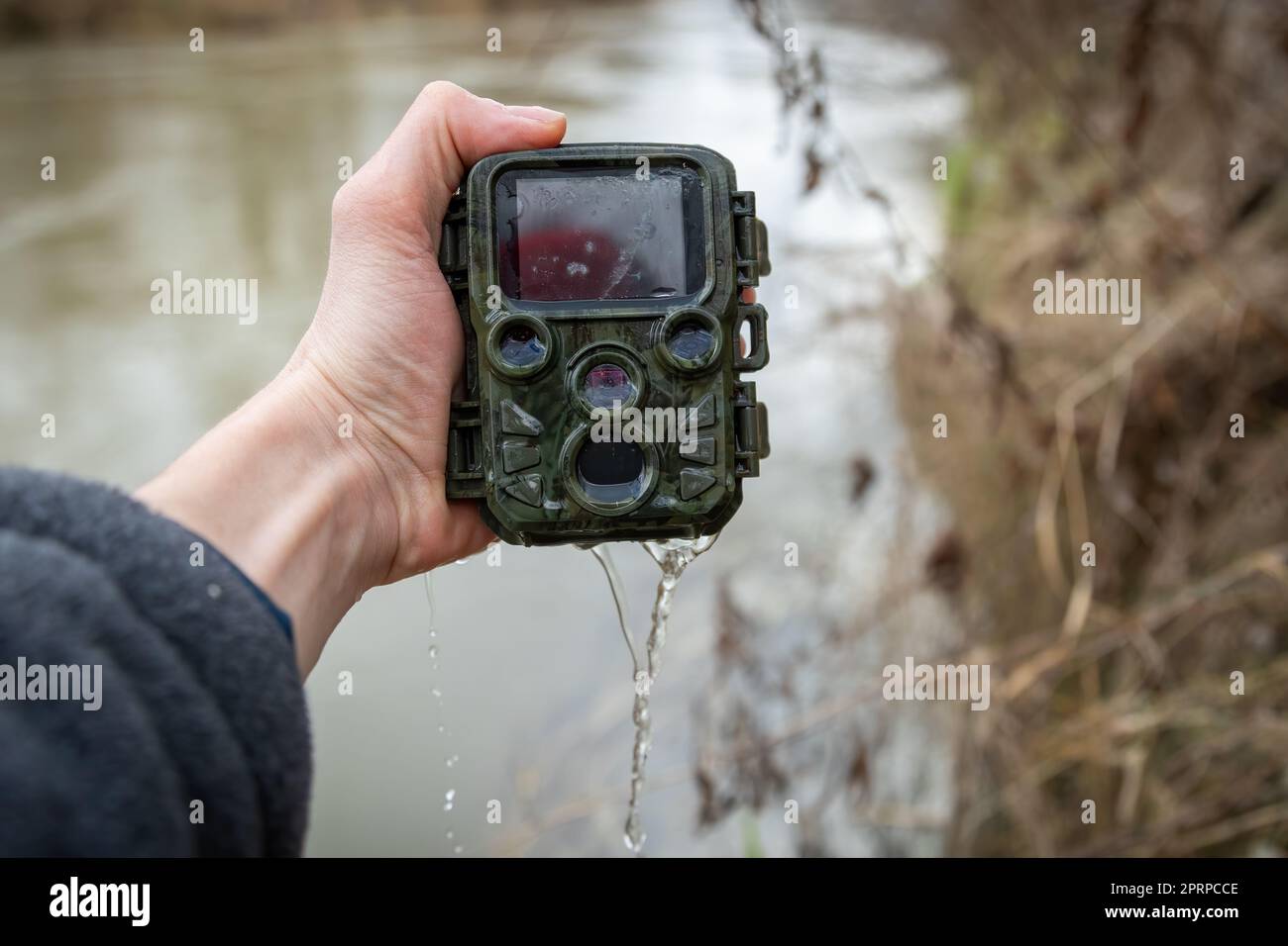 Hand holding a drowned trail camera near river with water leaking in ...