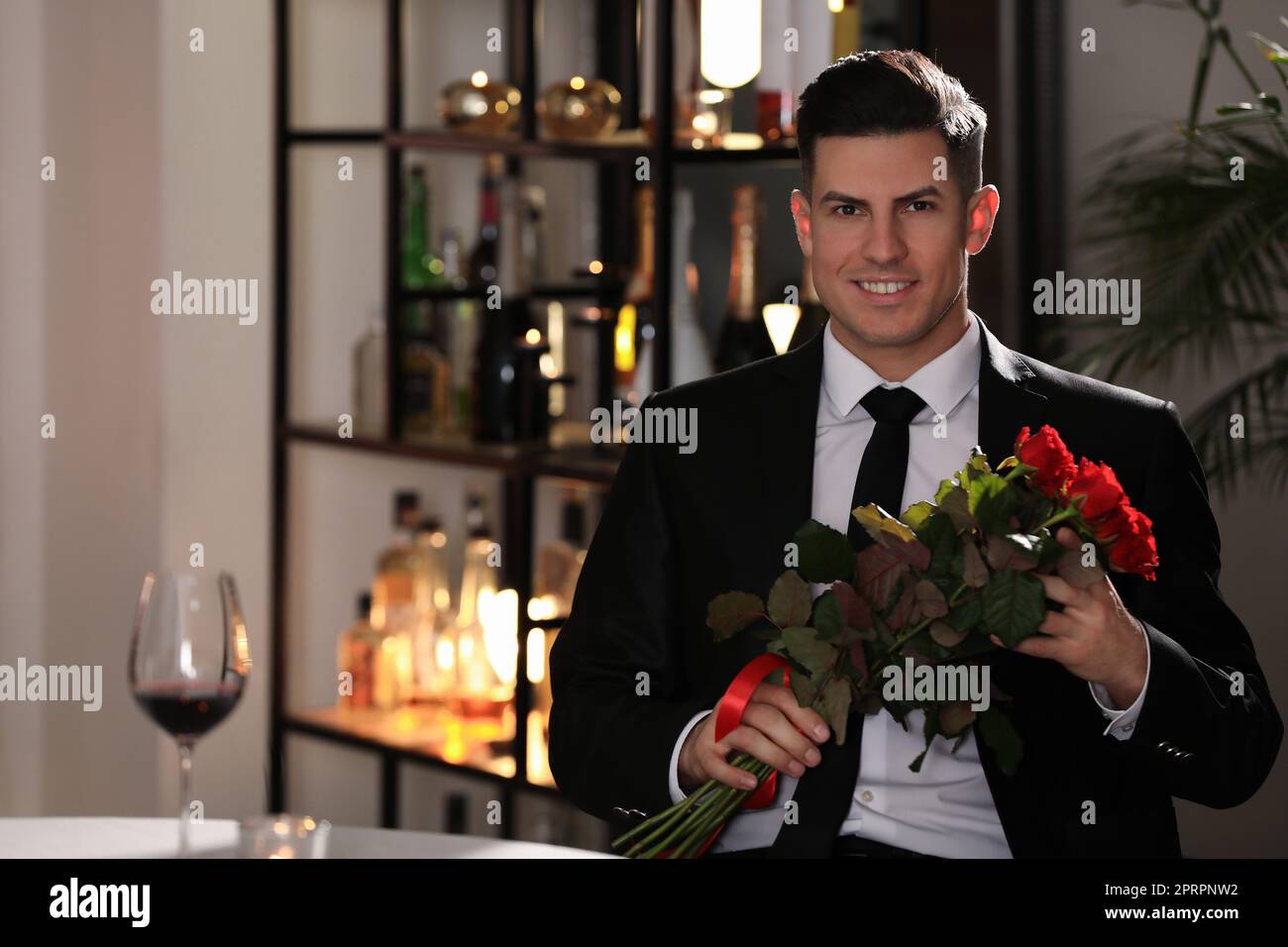 Happy man with roses waiting for his girlfriend in restaurant on ...