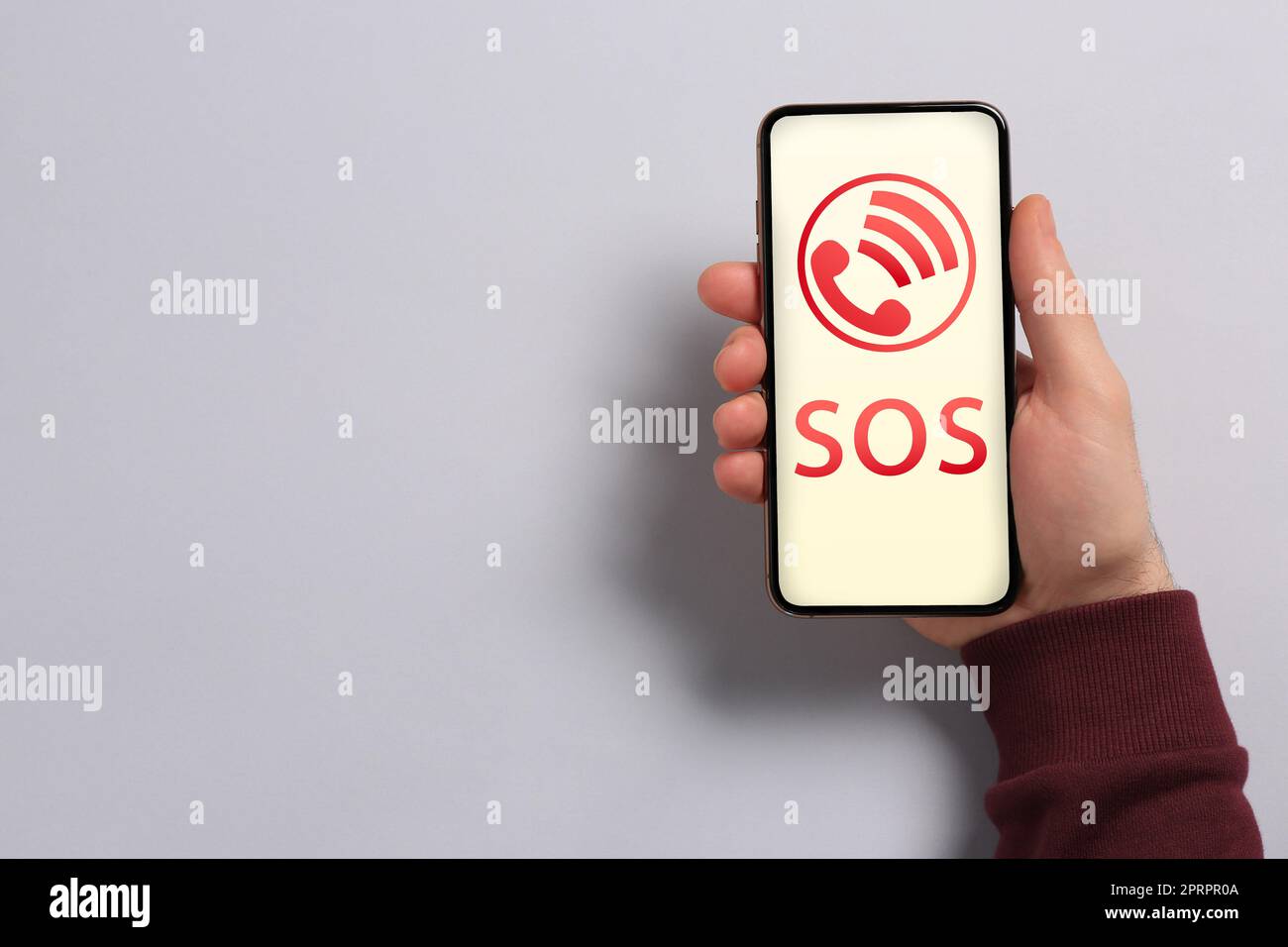 Man holding smartphone with emergency call SOS on screen on light grey ...