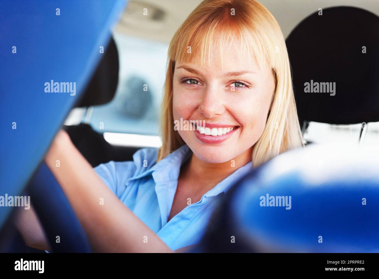 Cute blond female at the front seat driving a car. Closeup of a happy ...