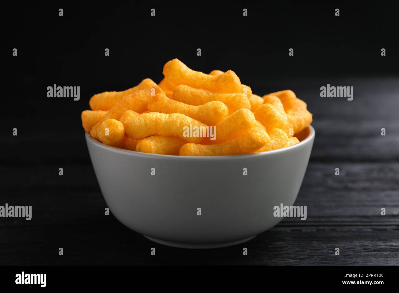 Bowl with crunchy cheesy corn snack on black wooden table, closeup ...