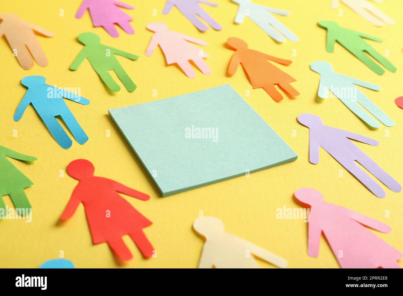 Many different paper human figures around blank card on yellow ...
