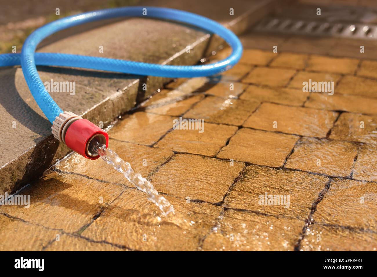 Water flowing from hose on stone floor outdoors, closeup. Space for ...