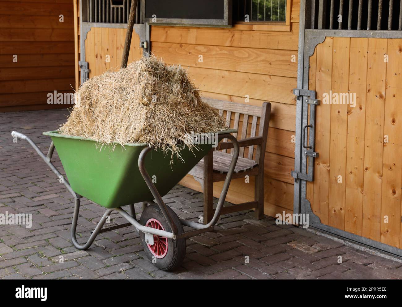 Wheelbarrow with hay near wooden stable outdoors Stock Photo - Alamy