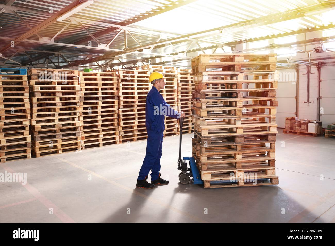 Worker moving wooden pallets with manual forklift in warehouse Stock ...