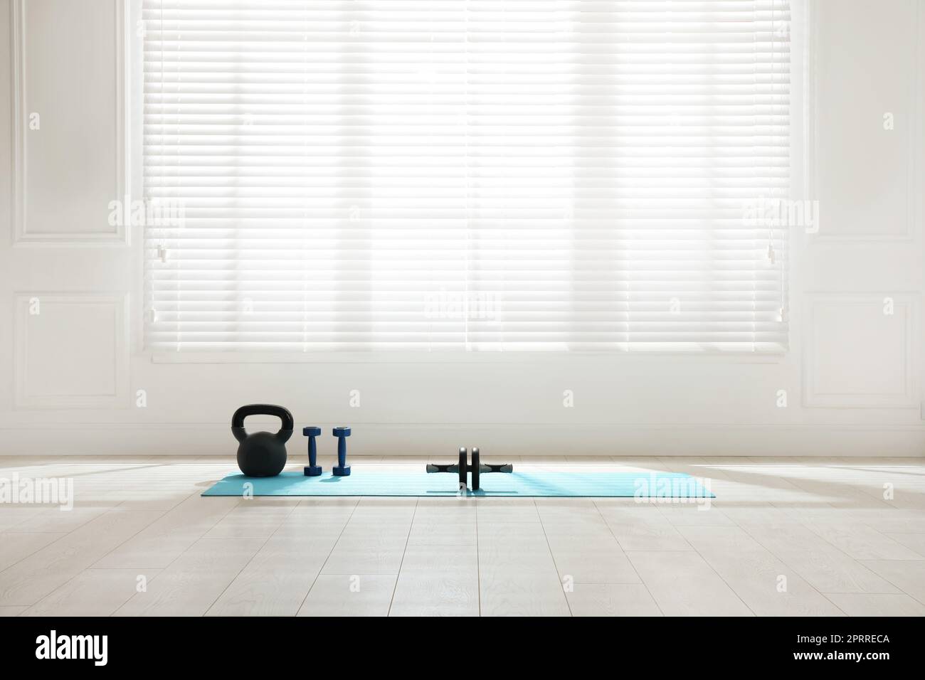 Exercise mat, ab roller, dumbbells and kettlebell near window in ...