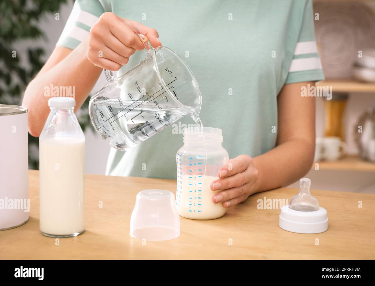 Woman preparing infant formula at table indoors, closeup. Baby milk ...