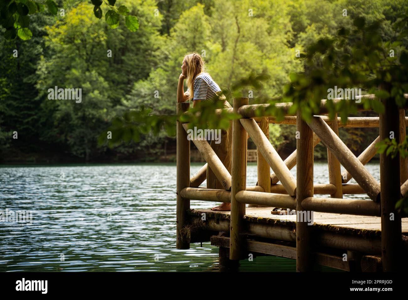 Caucasian blonde woman relaxing on wooden dock by a lake surrounded by ...