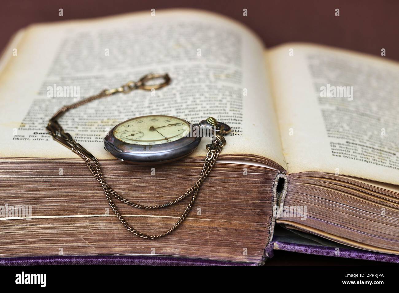 An antique pocket watch leans against an old book with yellowed pages ...