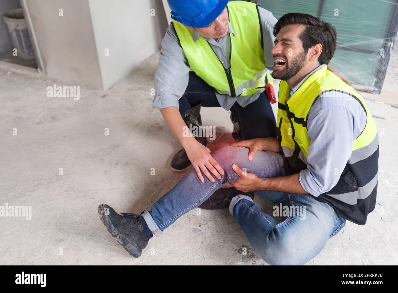 Young caucasian man in safety vest gripped his knee and screams in pain ...