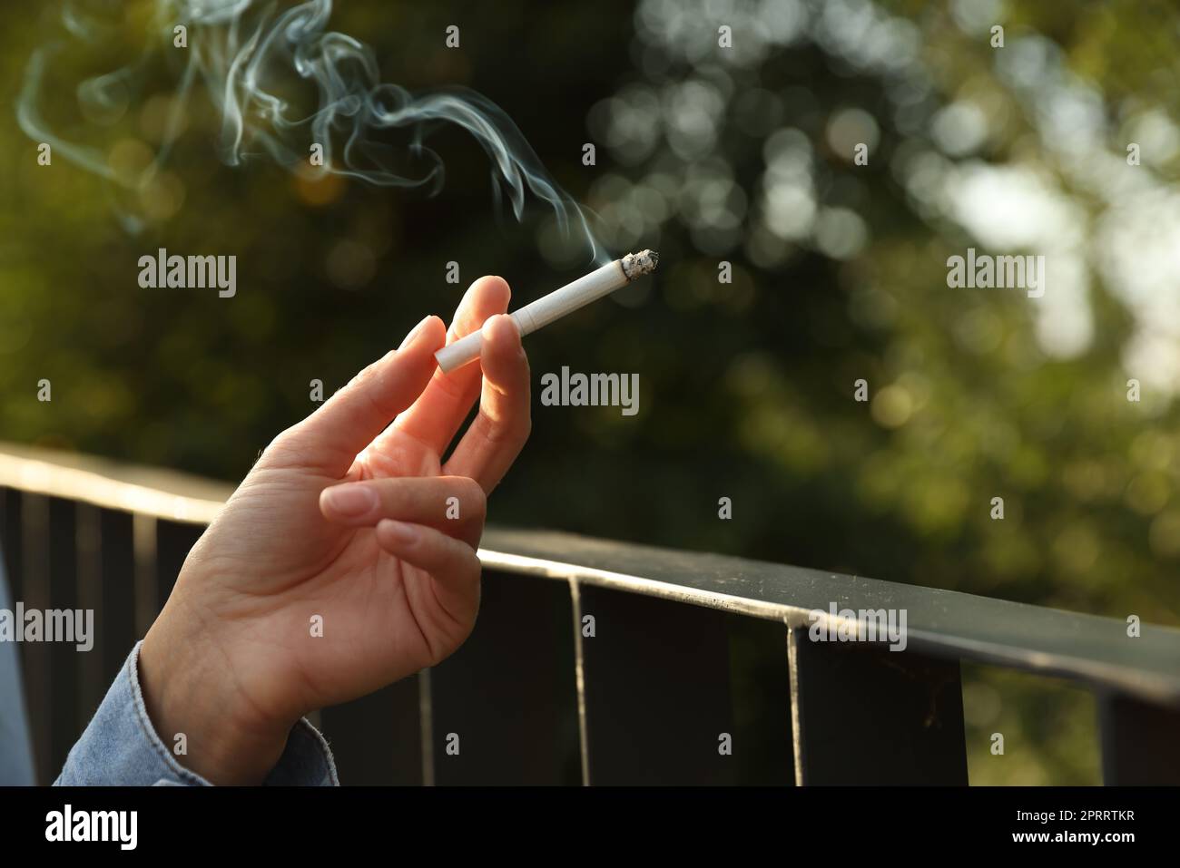 Woman smoking cigarette near railing outdoors, closeup of hand. Space ...