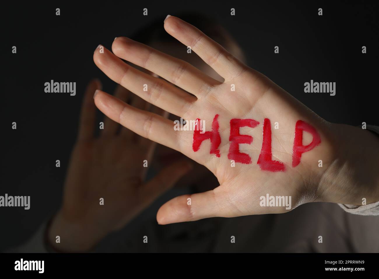 Woman with word Help written on hand against black background, closeup ...