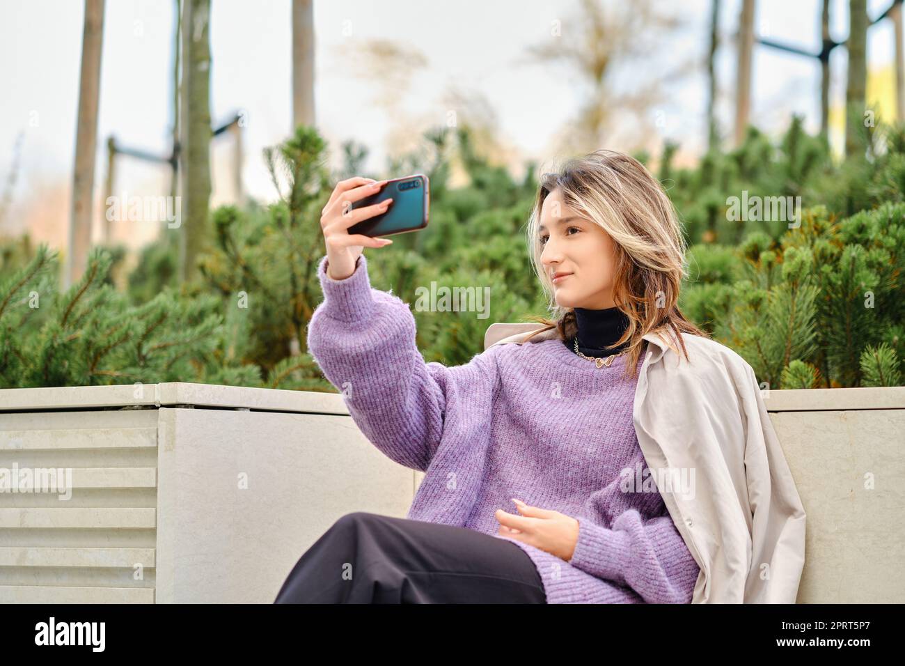 Cute young woman makes selfie or video call while sitting on bench in ...