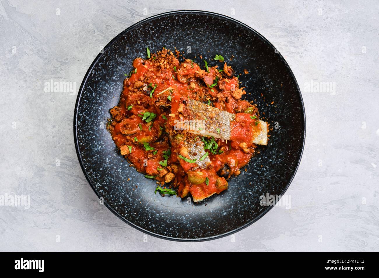 Top view of roasted zander served with steamed tomato, onion and olive ...