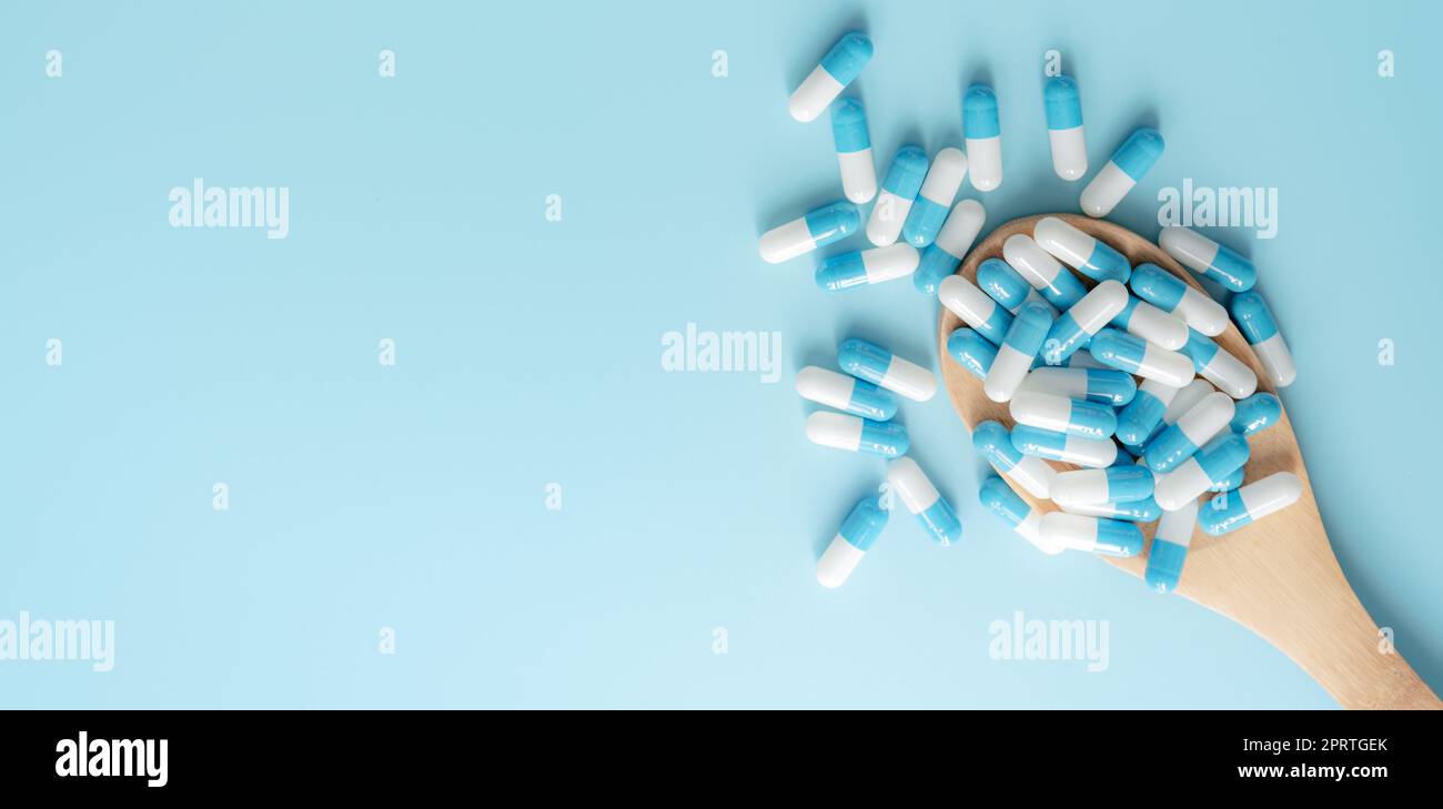 Top view of blue-white antibiotic capsule pills on wooden spoon and ...