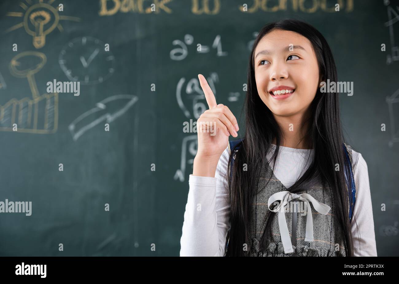 Asian school girl in uniform with backpack on classroom pointing up ...