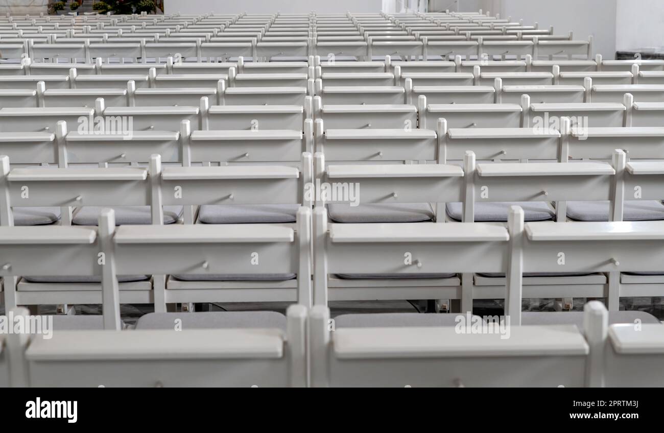 Many empty white benches stand in rows one behind the other as a ...