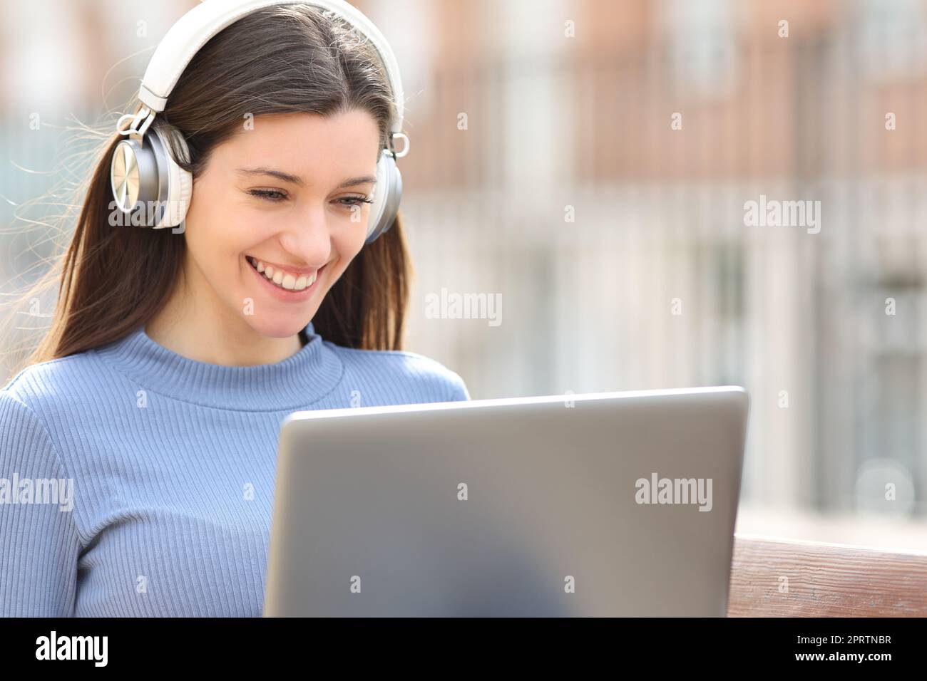 Happy woman using laptop with headphones in the street Stock Photo - Alamy