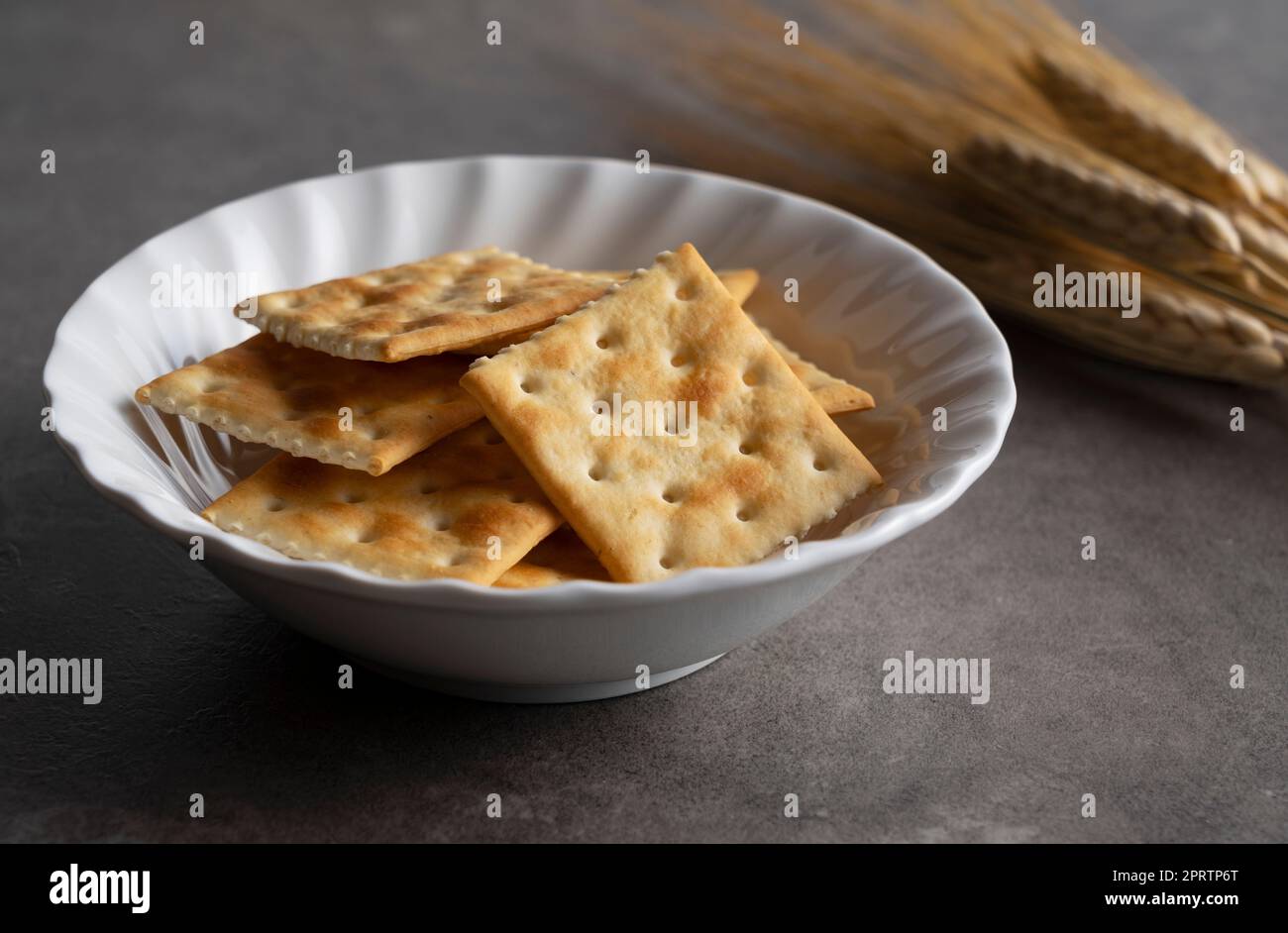 Crackers and ears of wheat in a dish set against a dark stone ...