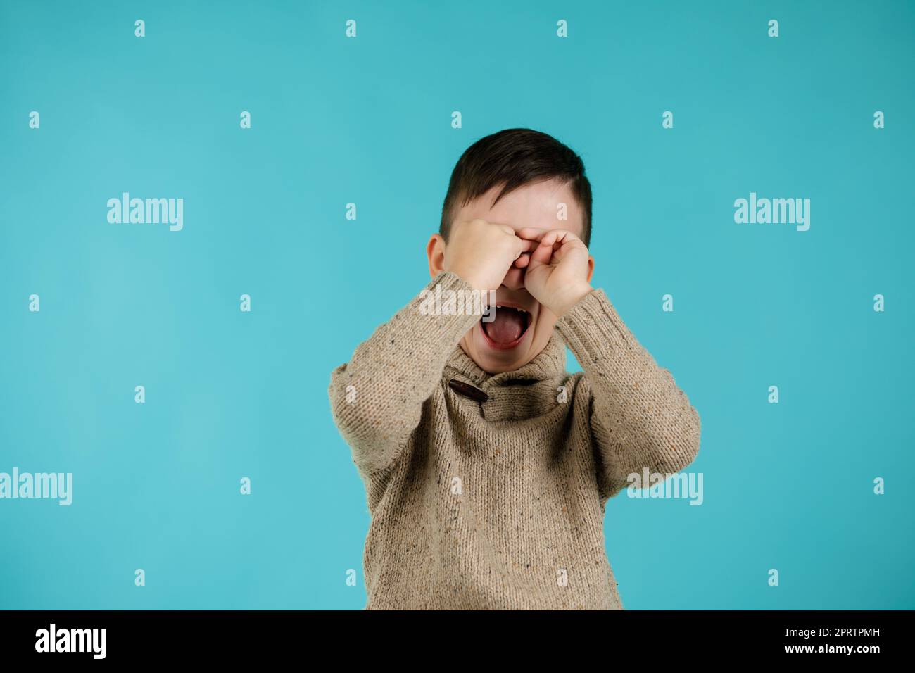 upset little child boy in sweater is crying on blue background. boy ...