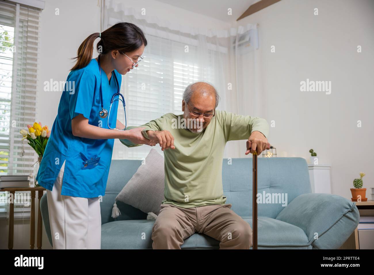 Caring nurse helping supporting senior disabled man to stand up with walking stick, young woman ...