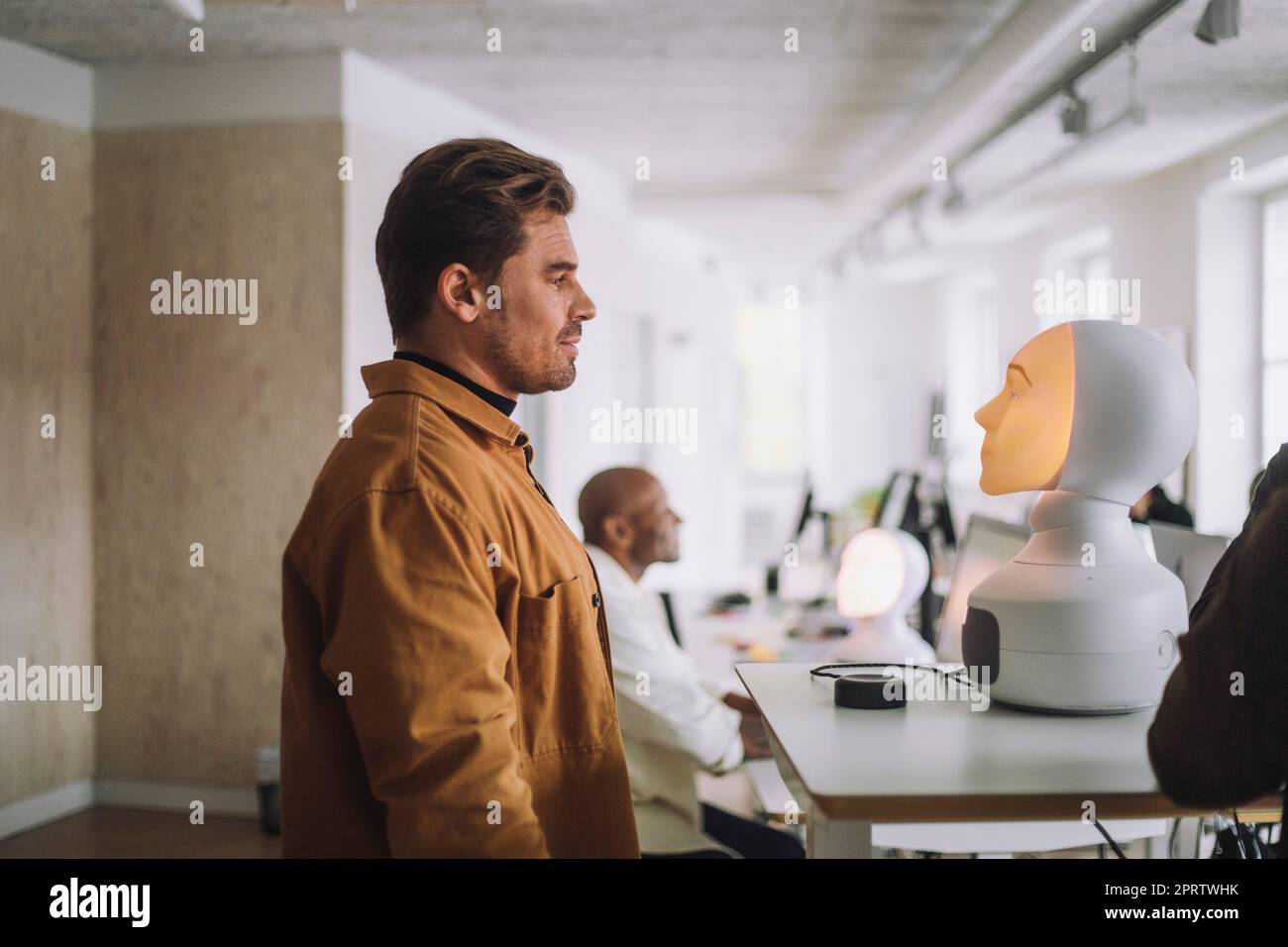 Side view of smiling PhD student standing in front of social robot in ...
