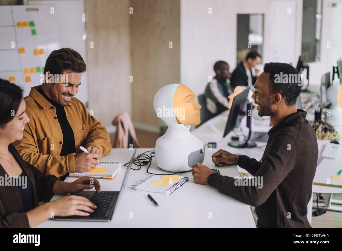 Happy PhD students planning by robot at desk in innovation lab Stock ...