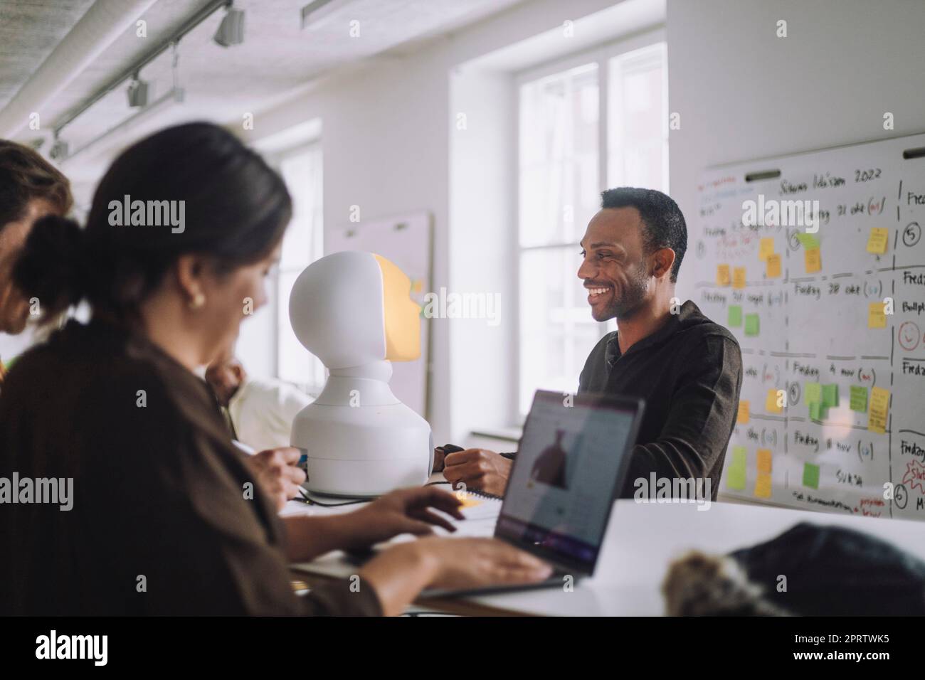 Smiling PhD student communicating with social robot at desk in ...