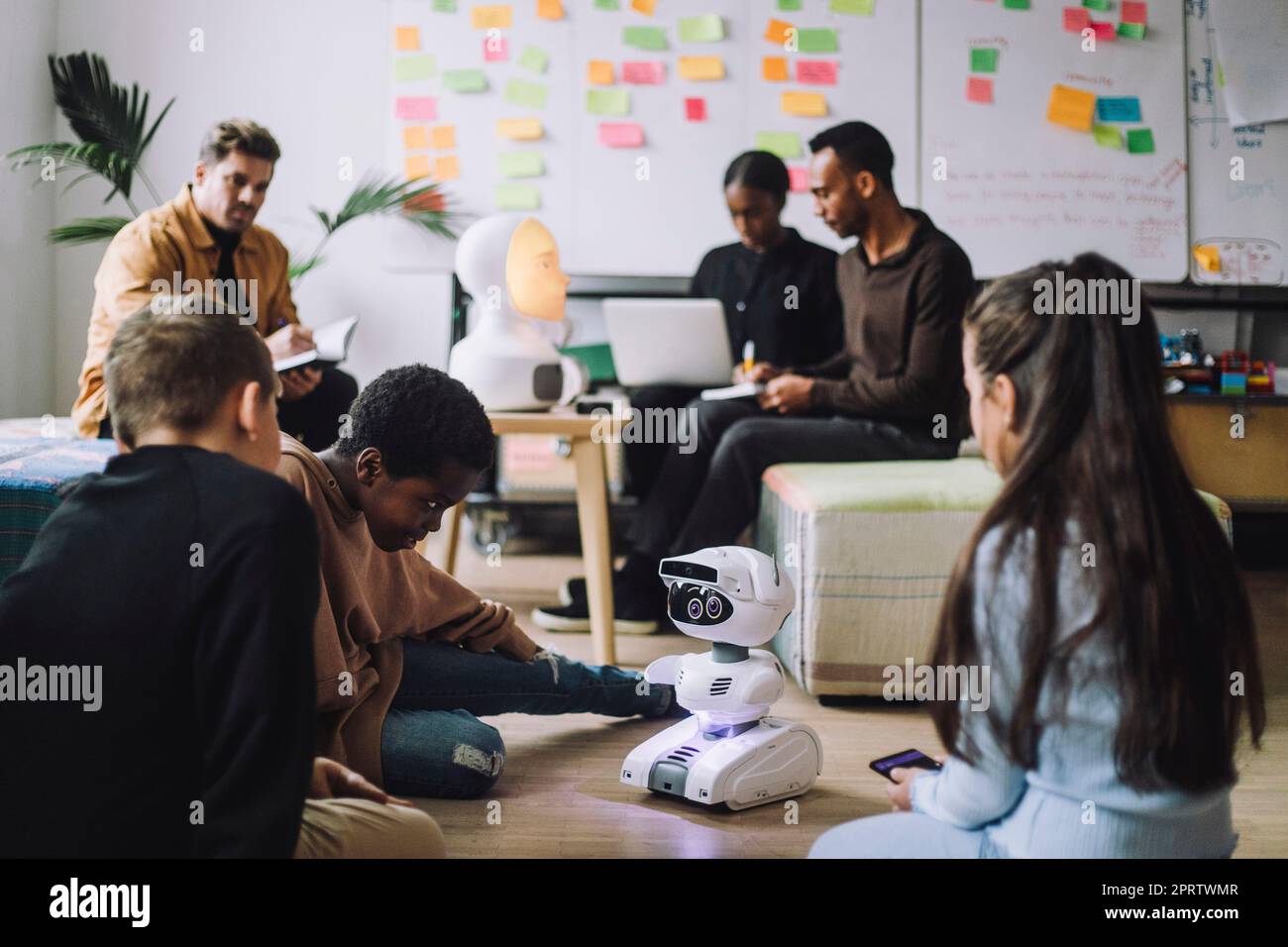 Multiracial boys and girl looking at futuristic robot on floor in ...