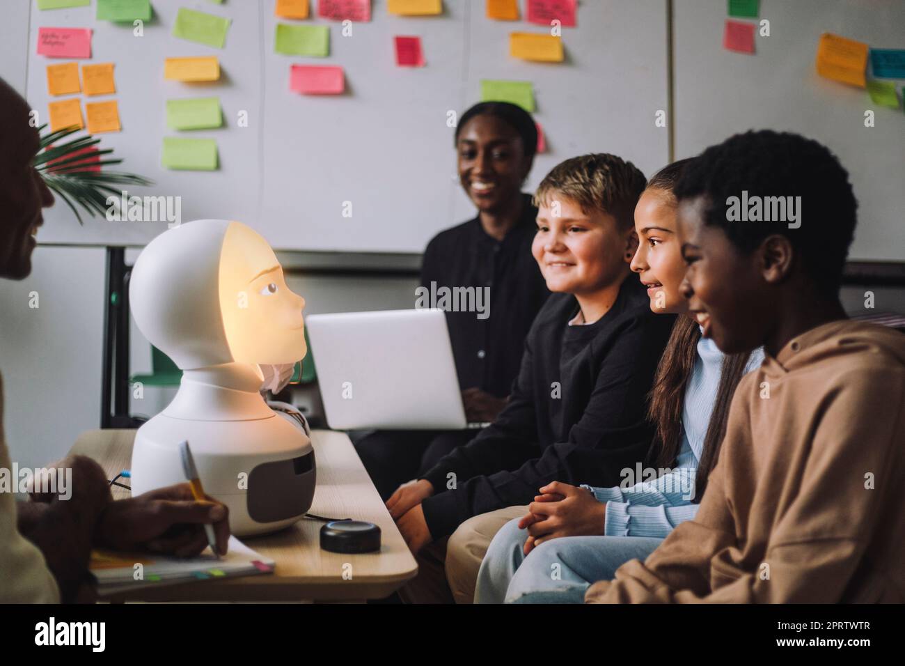 Smiling multiracial students looking at illuminated modern robot in ...