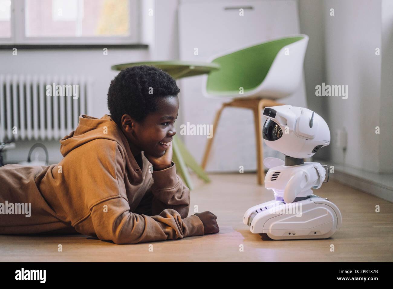 Smiling boy talking with AI robot while lying on floor in innovation ...