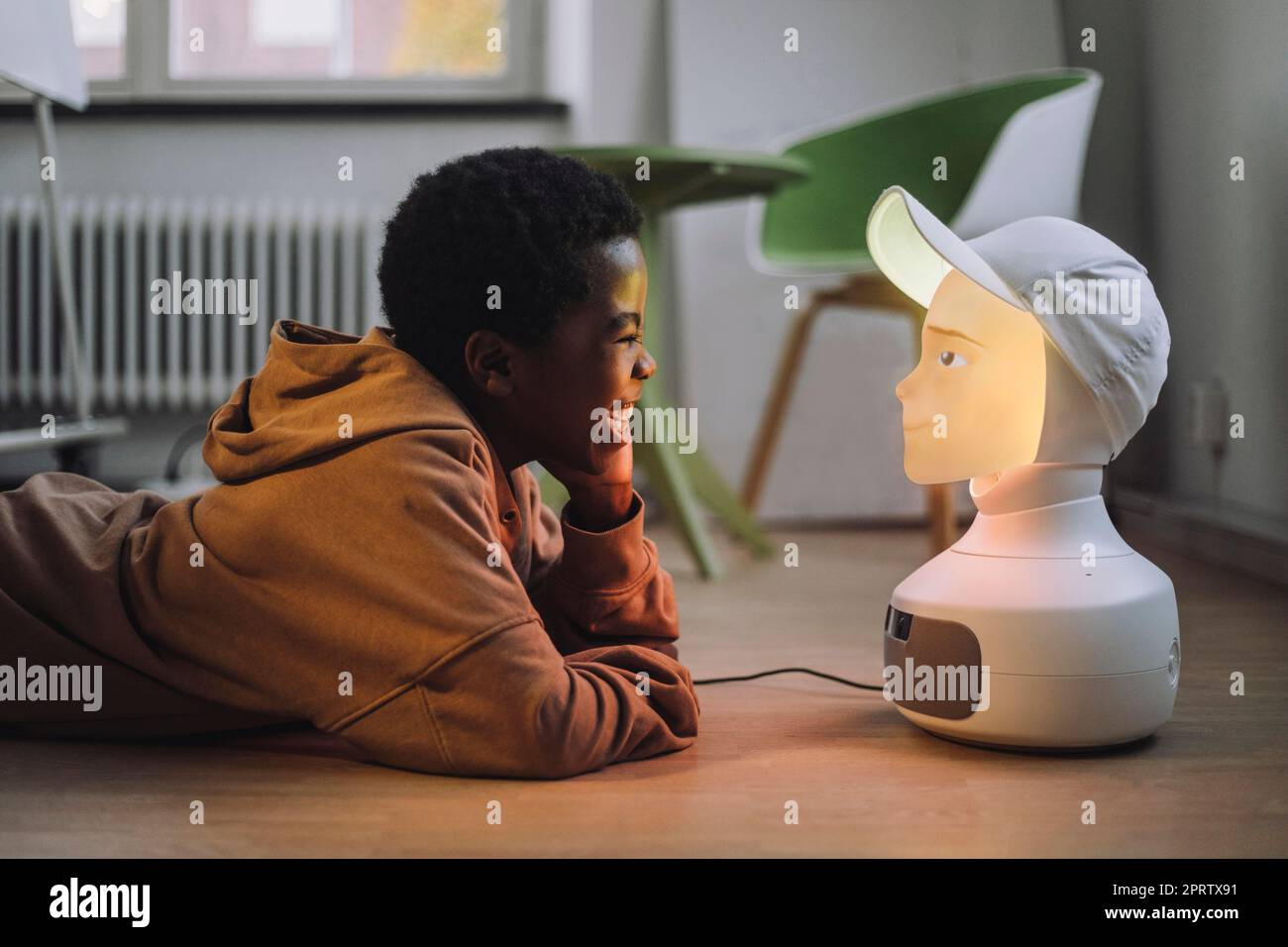 Cheerful boy in front of illuminated AI robot while lying on floor in ...