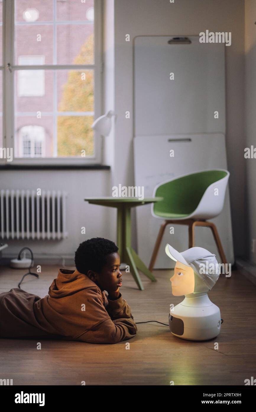 Boy talking with illuminated AI robot while lying on floor in ...